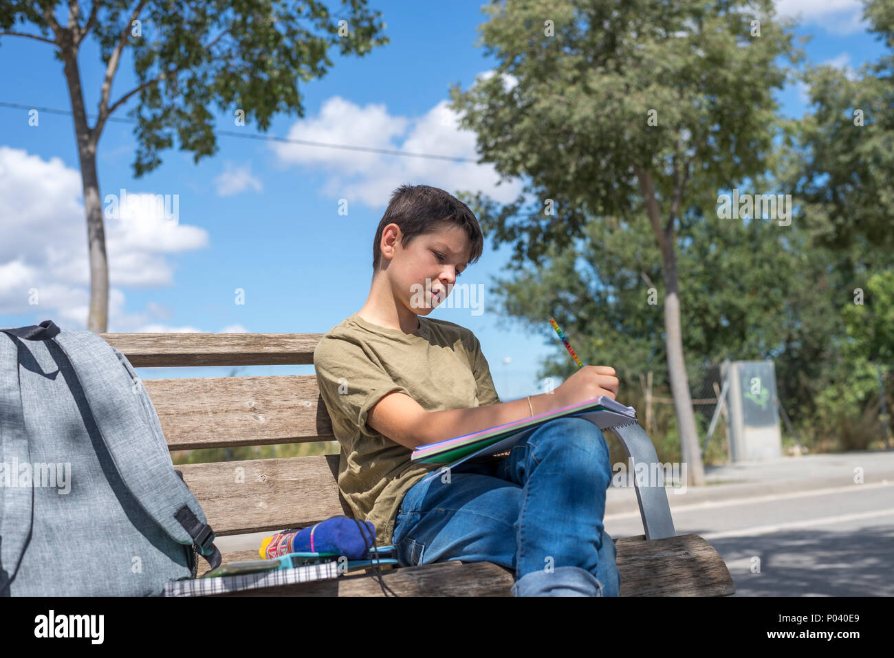 Portrait of a teenager boy sitting on a wood park bench doing his ...