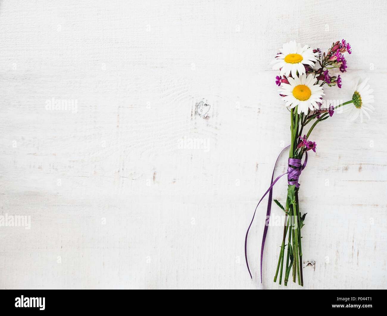 Bouquet of wildflowers, tied with a purple ribbon, on a white, vintage ...