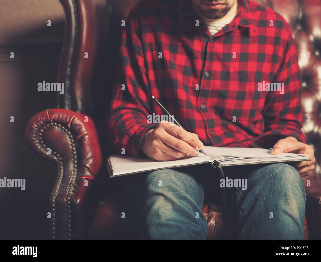 A young man sitting on a leather sofa is writing in a notebook Stock ...