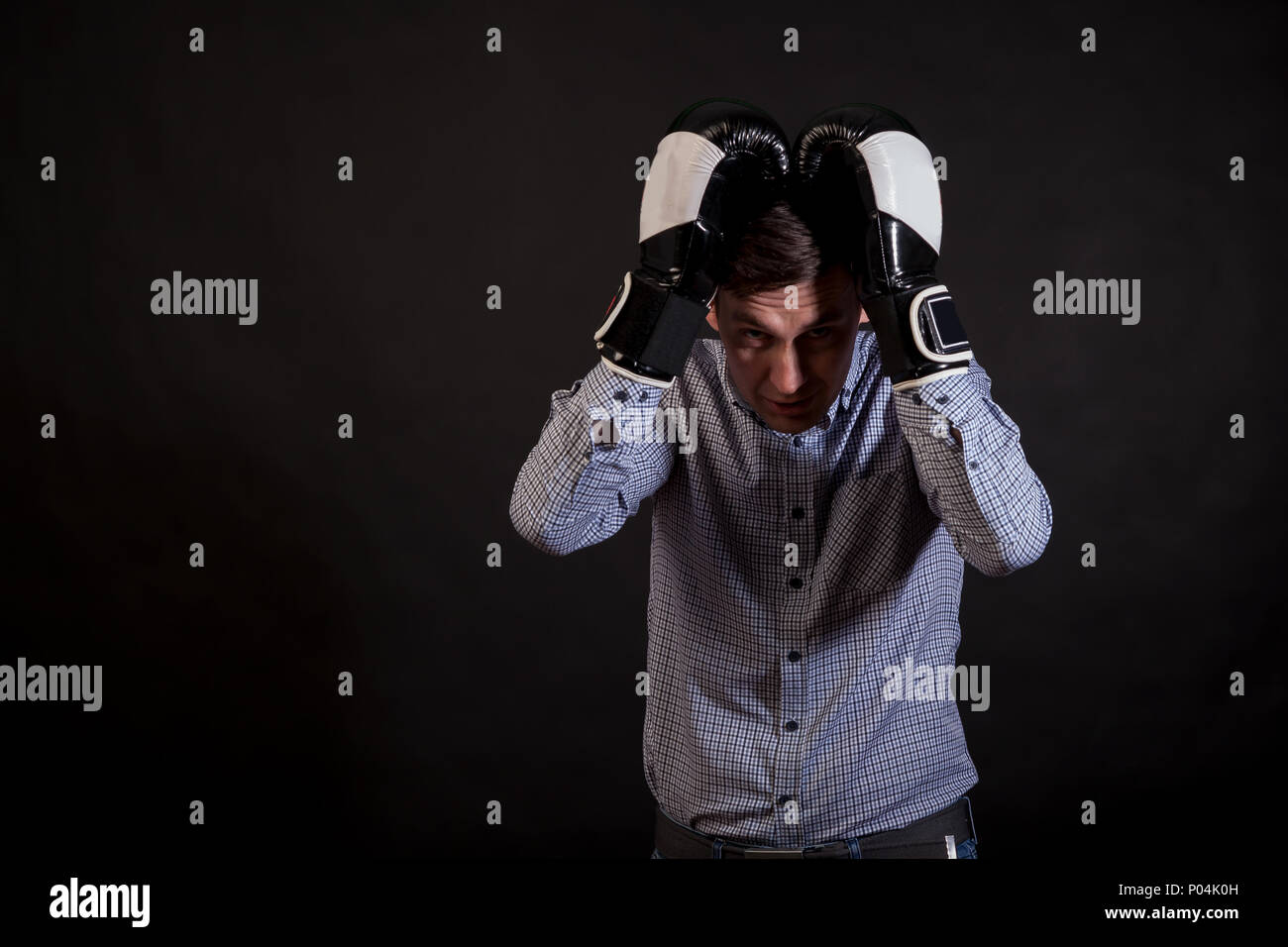 Dark-haired man in a plaid shirt with boxing gloves on his hands clings ...