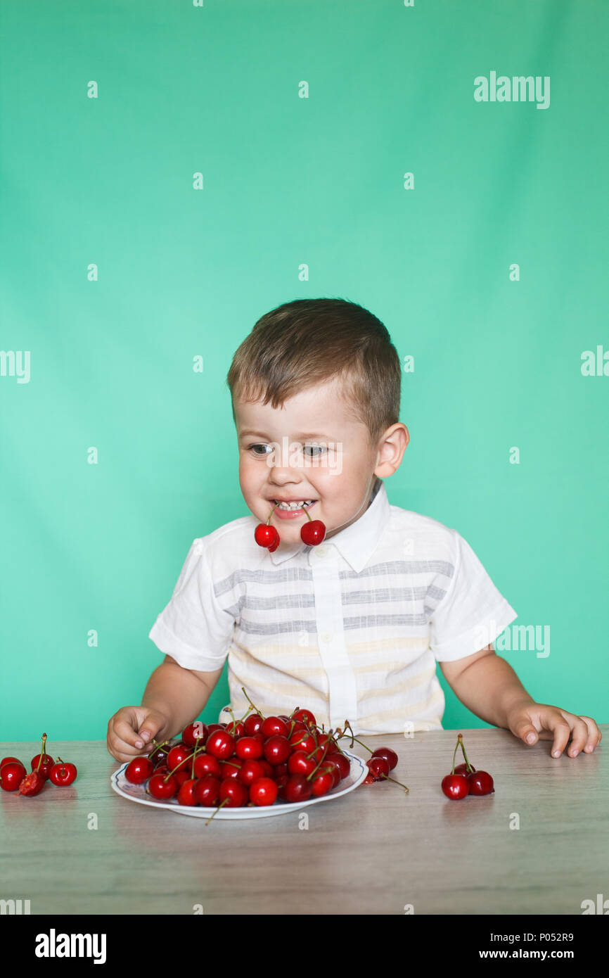 A little boy eating ripe cherries. Little Boy On A Green Background ...