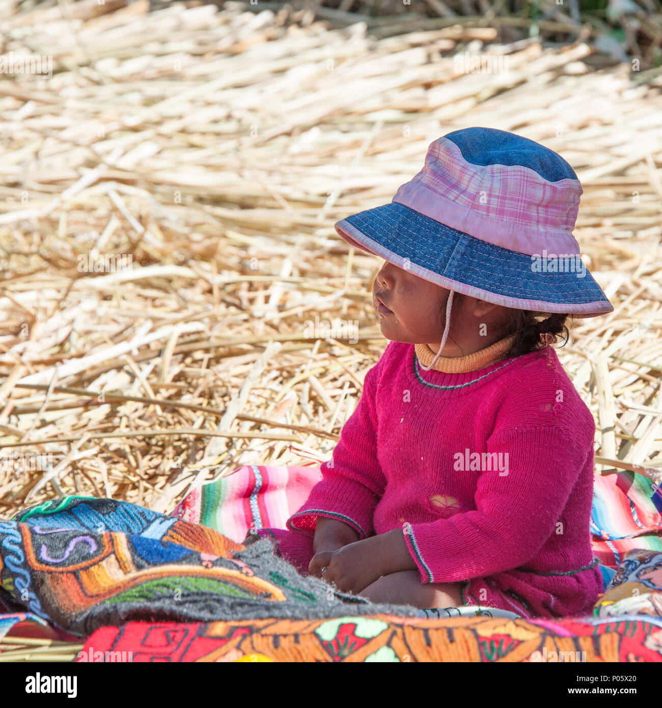 A local peruvian child sits in the sun, on the reeds, the floating ...