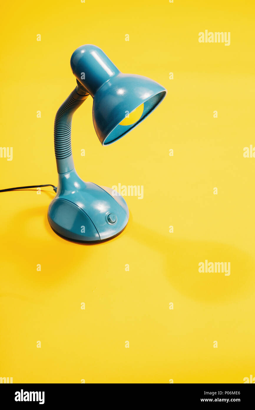 Blue desk lamp with yellow light bulb standing on a yellow background ...