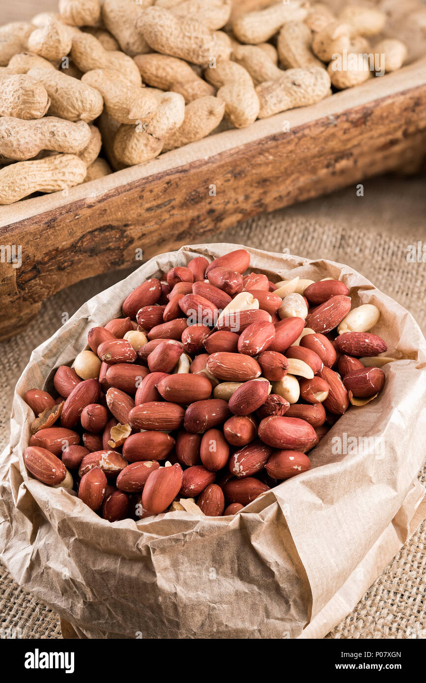 Paper bag full of peeled peanuts and peanuts in nutshell on a piece of ...