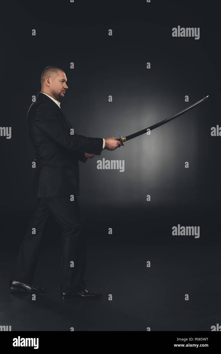 side view of mature man in suit with katana sword on dark background ...