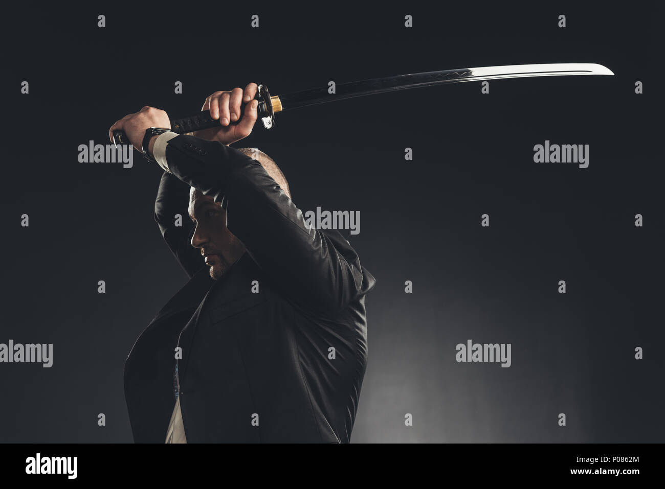 side view of man in suit making hit with katana sword isolated on black ...