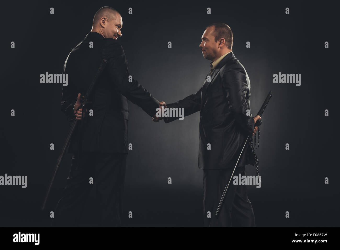 side view of businessmen shaking hands with katanas behind back ...