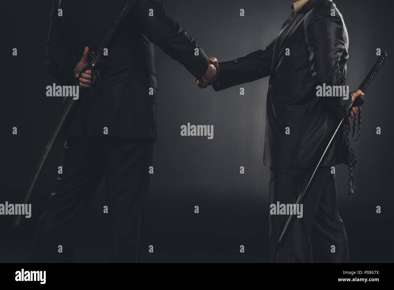 cropped shot of yakuza members shaking hands with katanas behind back ...