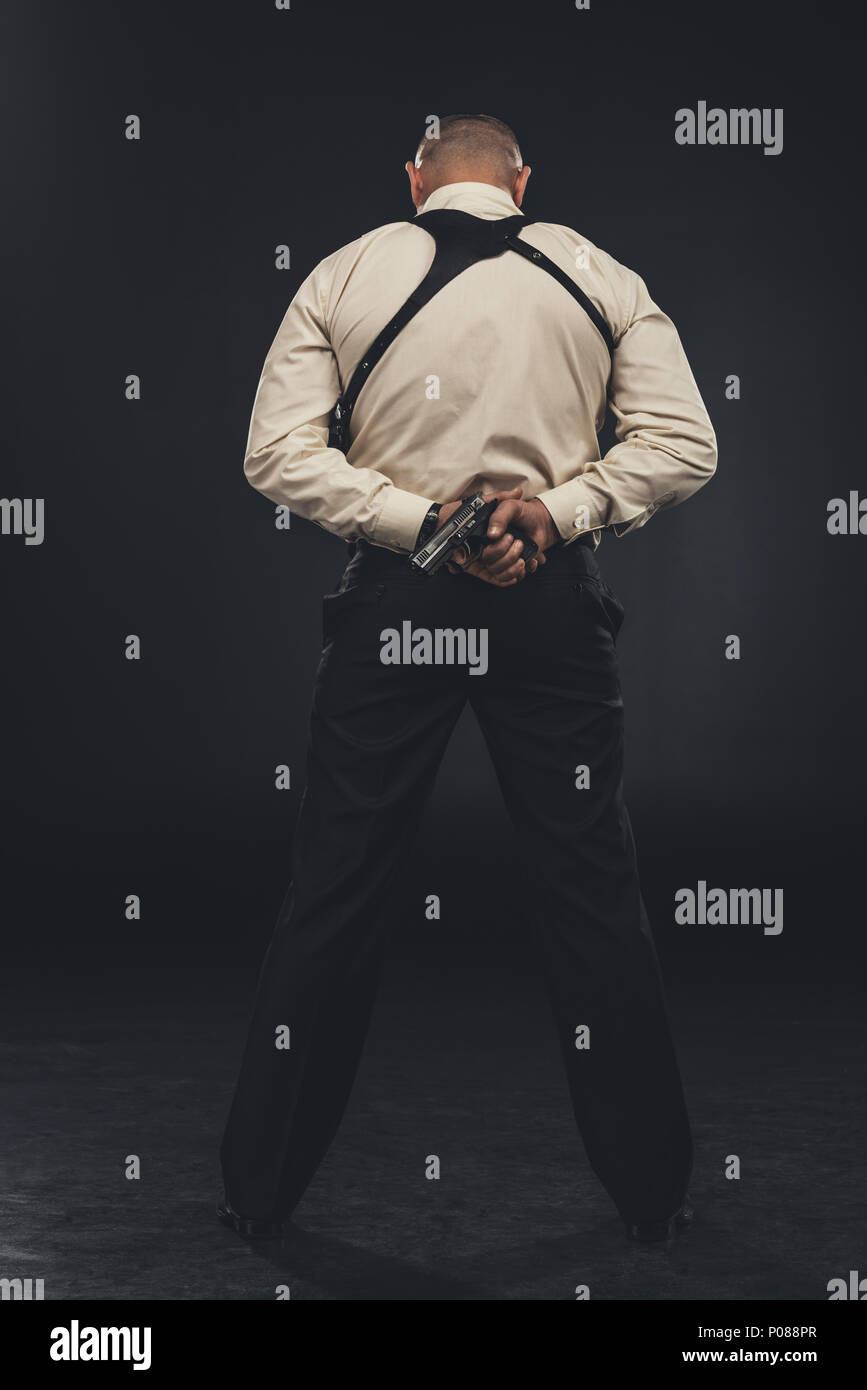 back view of killer in shirt holding gun behind back Stock Photo - Alamy