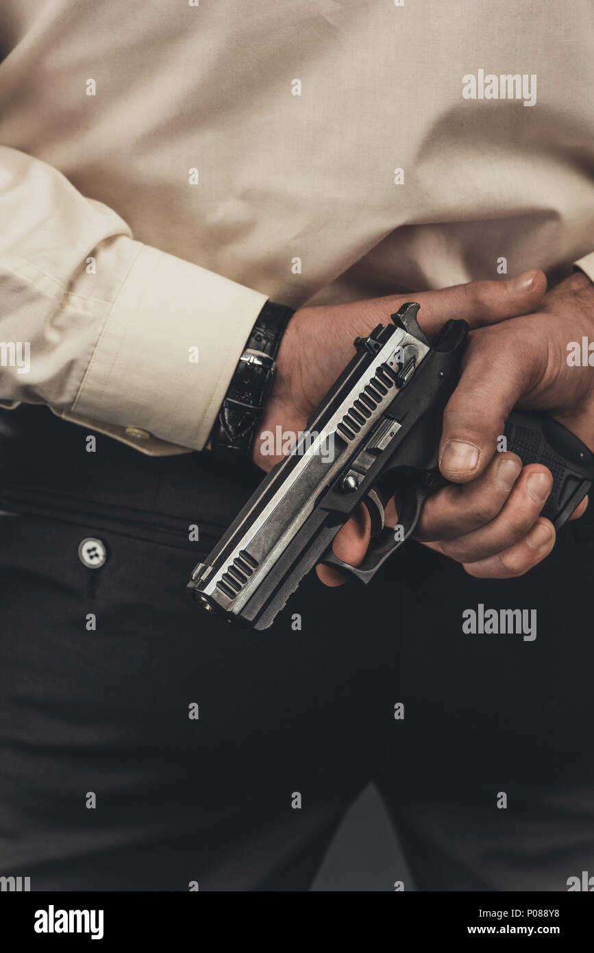 cropped shot of man in shirt holding gun behind back Stock Photo - Alamy