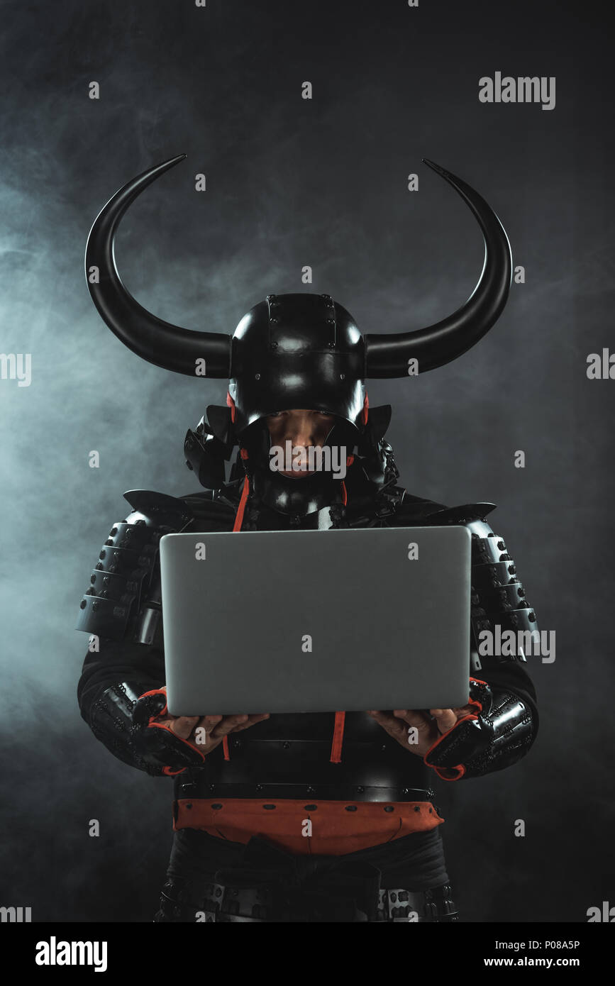 armored samurai warrior using laptop on dark background with smoke ...