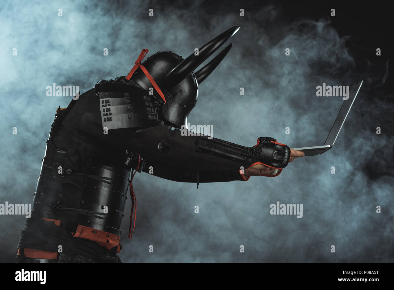 side view of armored samurai holding laptop on dark background with ...