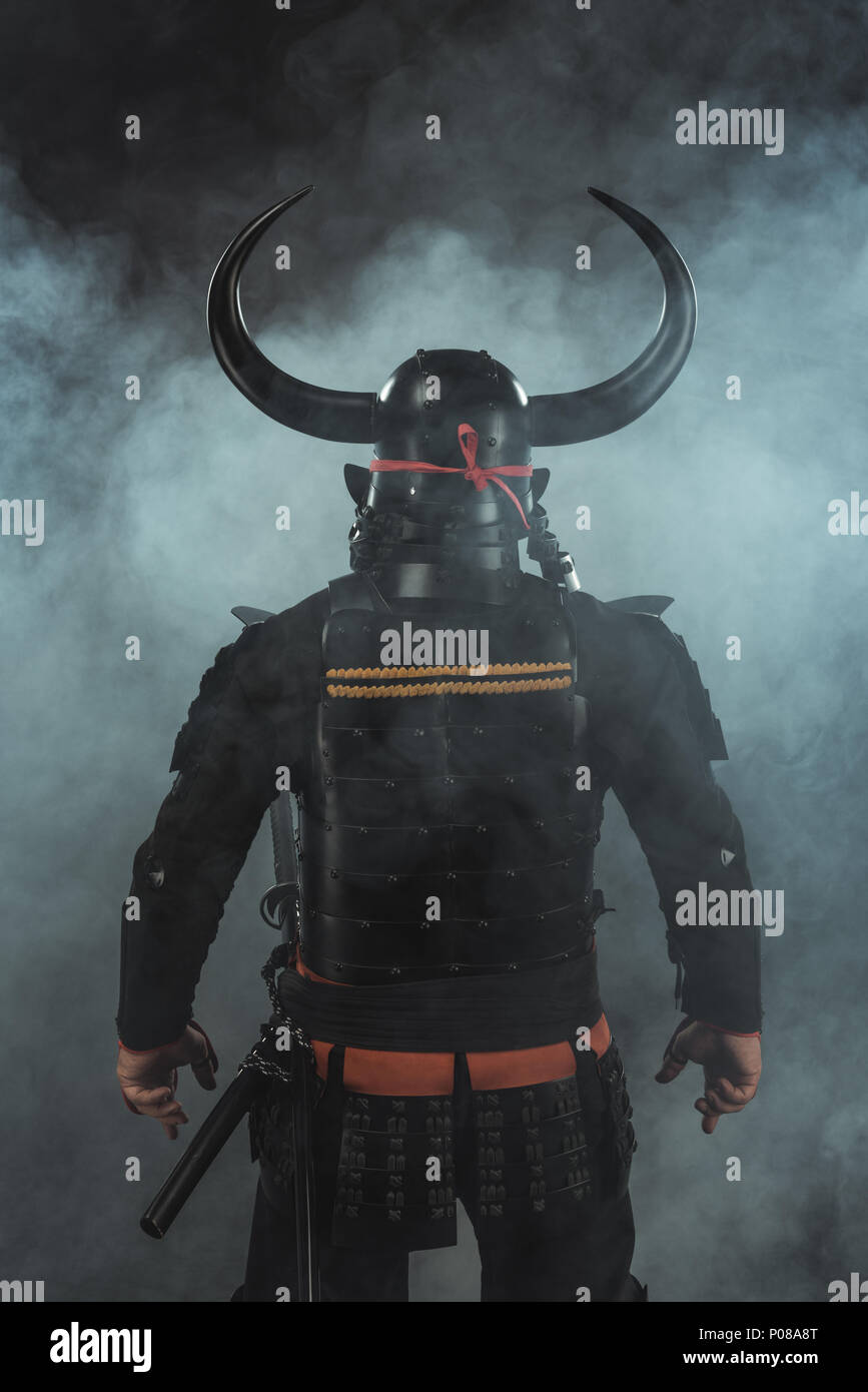back view of samurai in traditional armor and horned helmet on dark ...