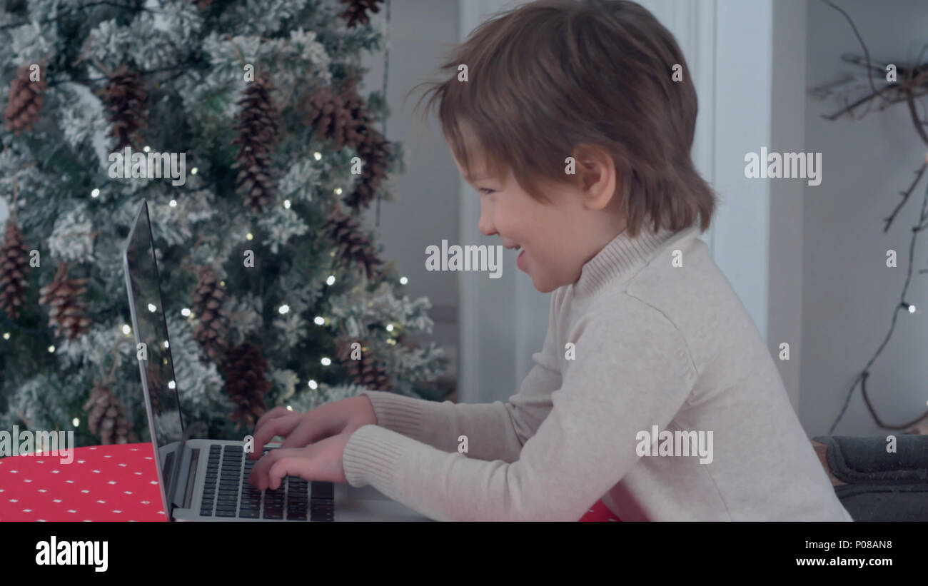 Smiling little boy typing letter to Santa Claus on a laptop near the ...