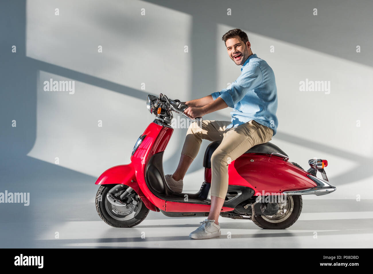 side view of young cheerful man sitting on red scooter Stock Photo - Alamy
