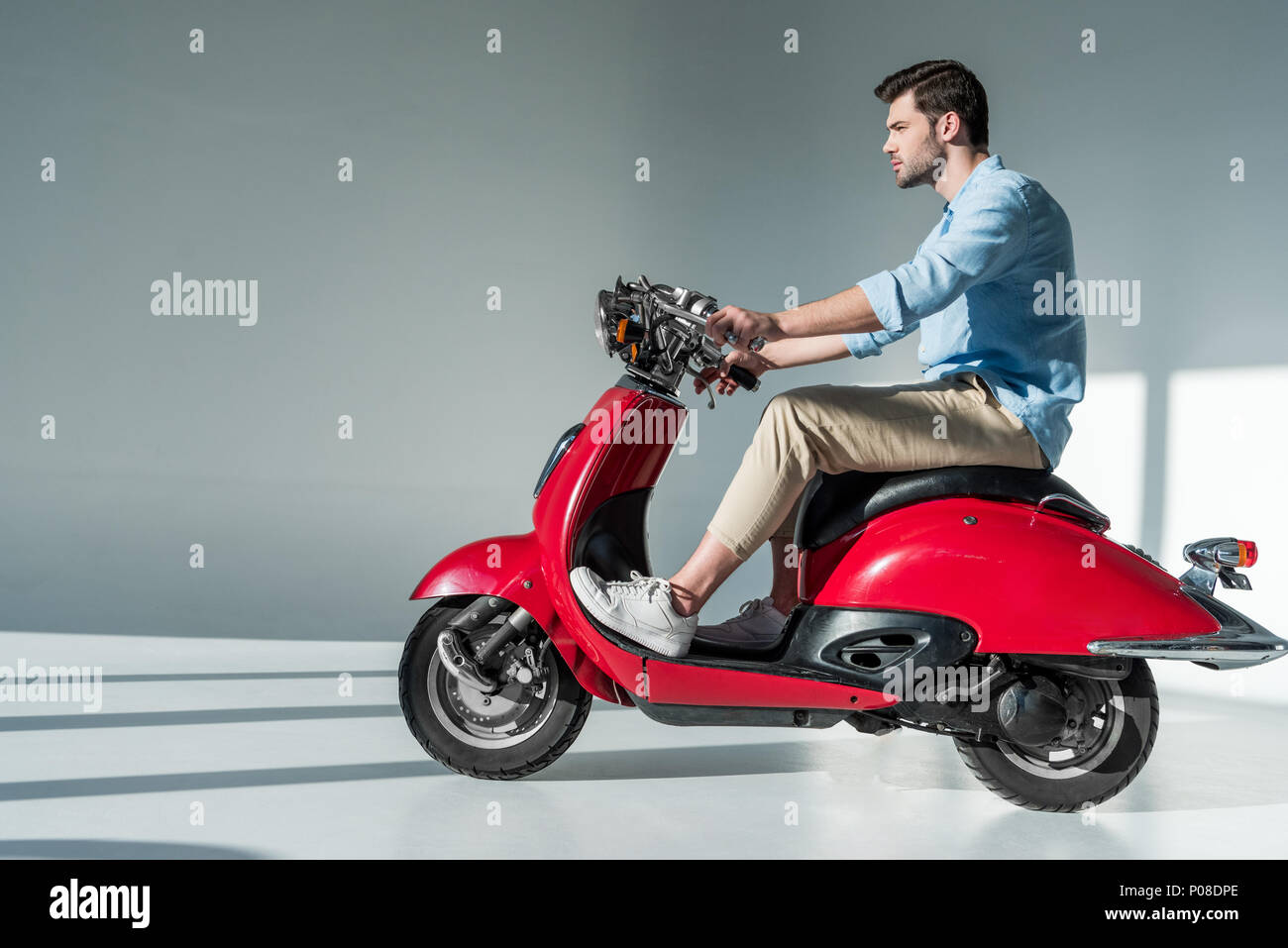 side view of fashionable young man riding red scooter Stock Photo - Alamy