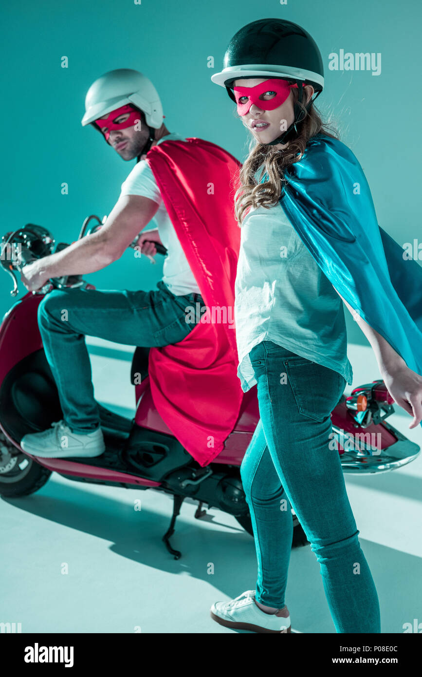 stylish couple in helmets and superhero costumes with red scooter ...