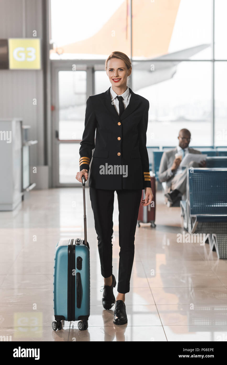 happy female pilot with suitcase walking by airport lobby Stock Photo ...