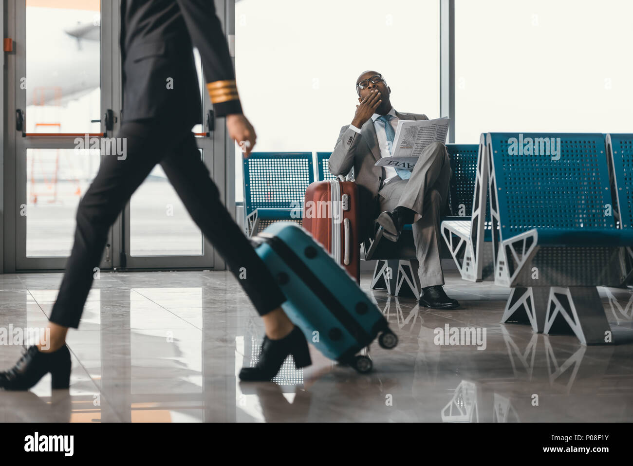 businessman waiting for flight at airport lobby while female pilot ...