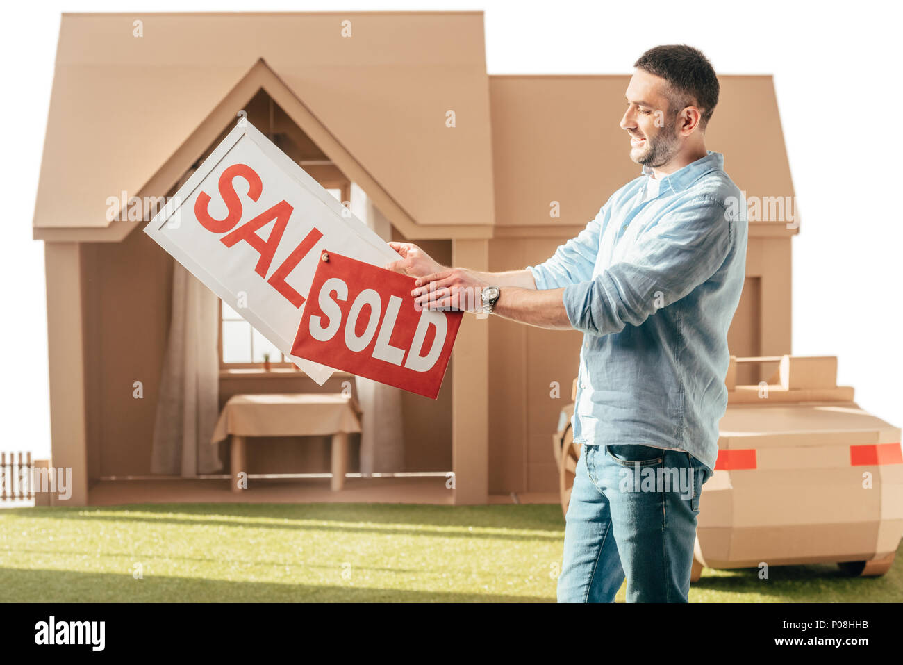man holding sale and sold signboards in front of cardboard house ...