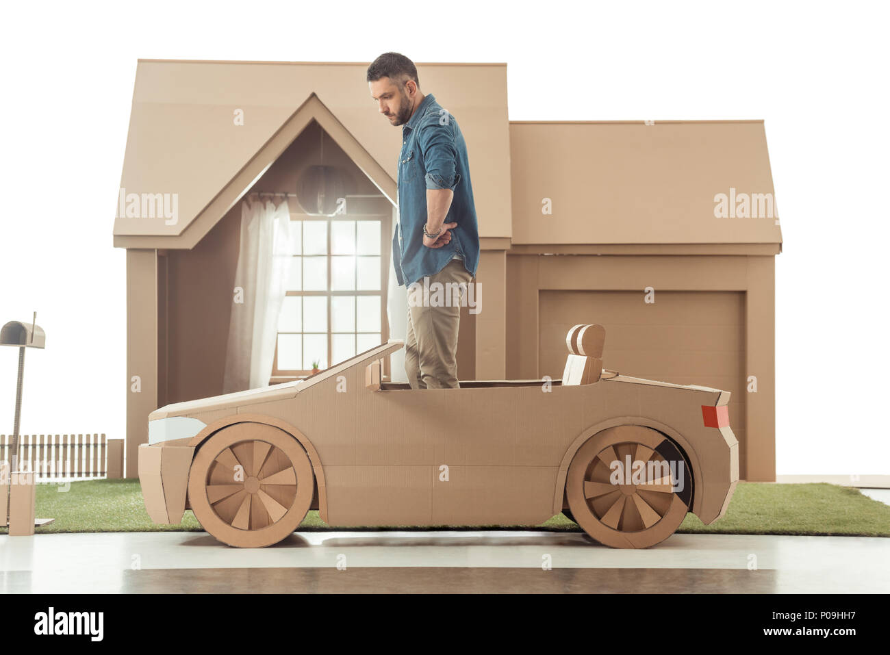 side view of man in cardboard car in front of cardboard house isolated ...