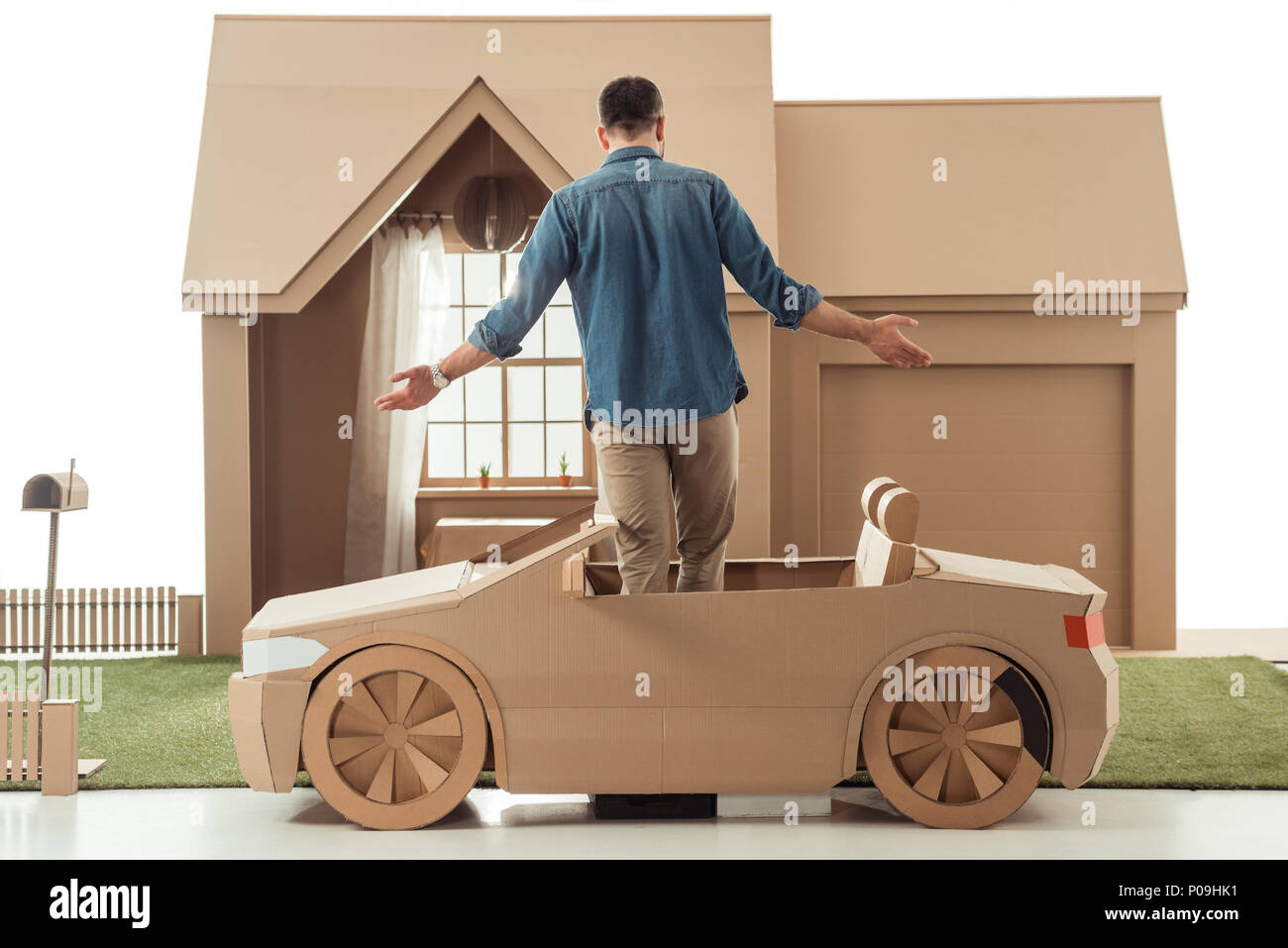 rear view of man in cardboard car in front of cardboard house isolated ...