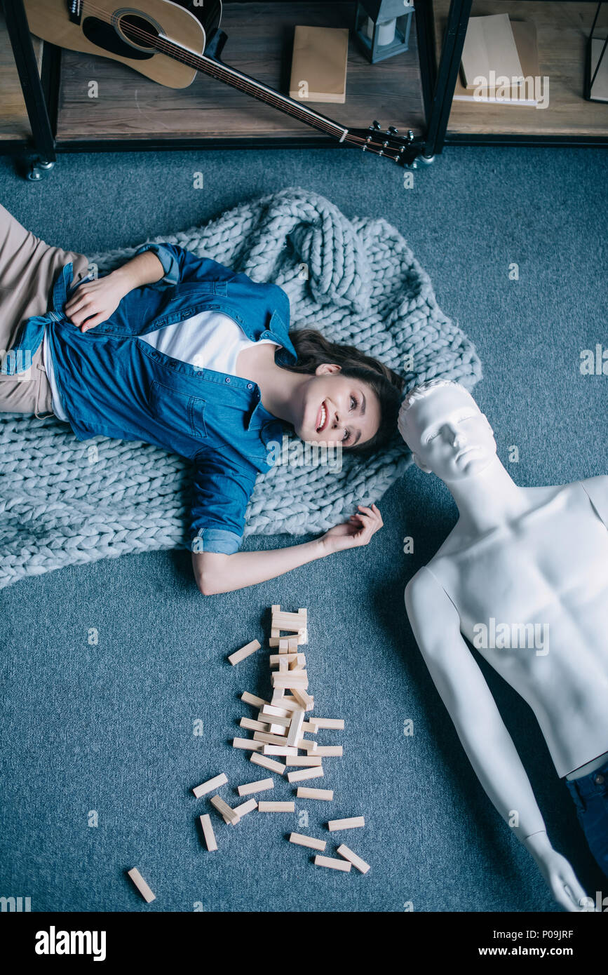 overhead view of woman and mannequin lying on floor near blocks wood ...