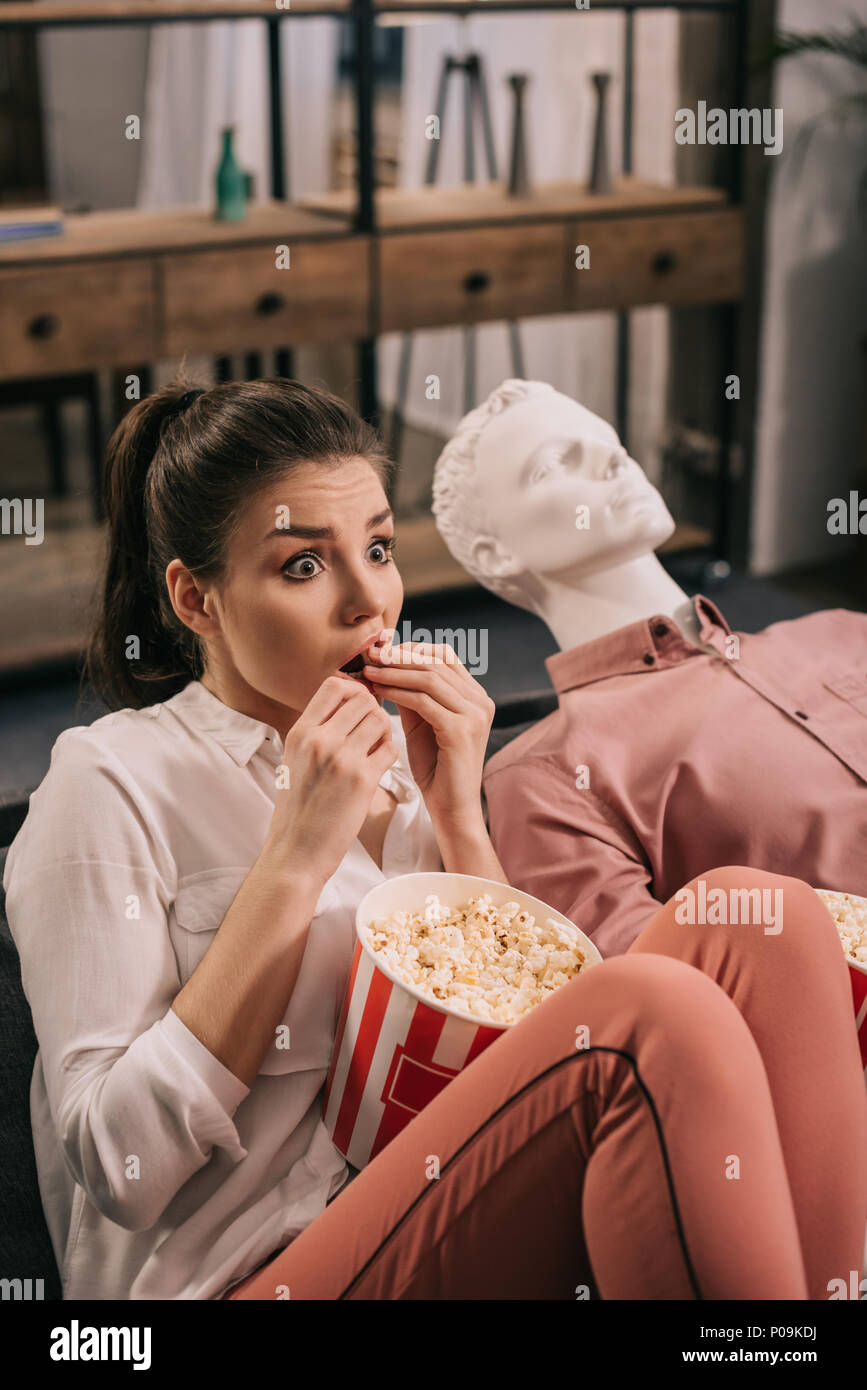 scared woman eating popcorn while watching film together with manikin ...
