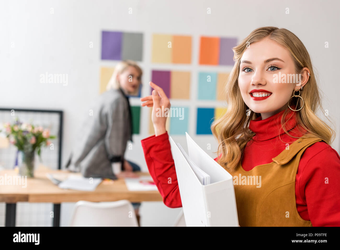 smiling magazine editor with folder in modern office with colleague and ...