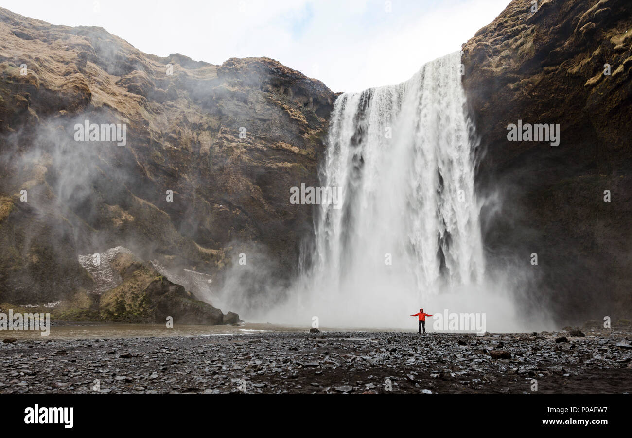 Hiker with red jacket in front of a high waterfall Skogafoss, Skogar ...