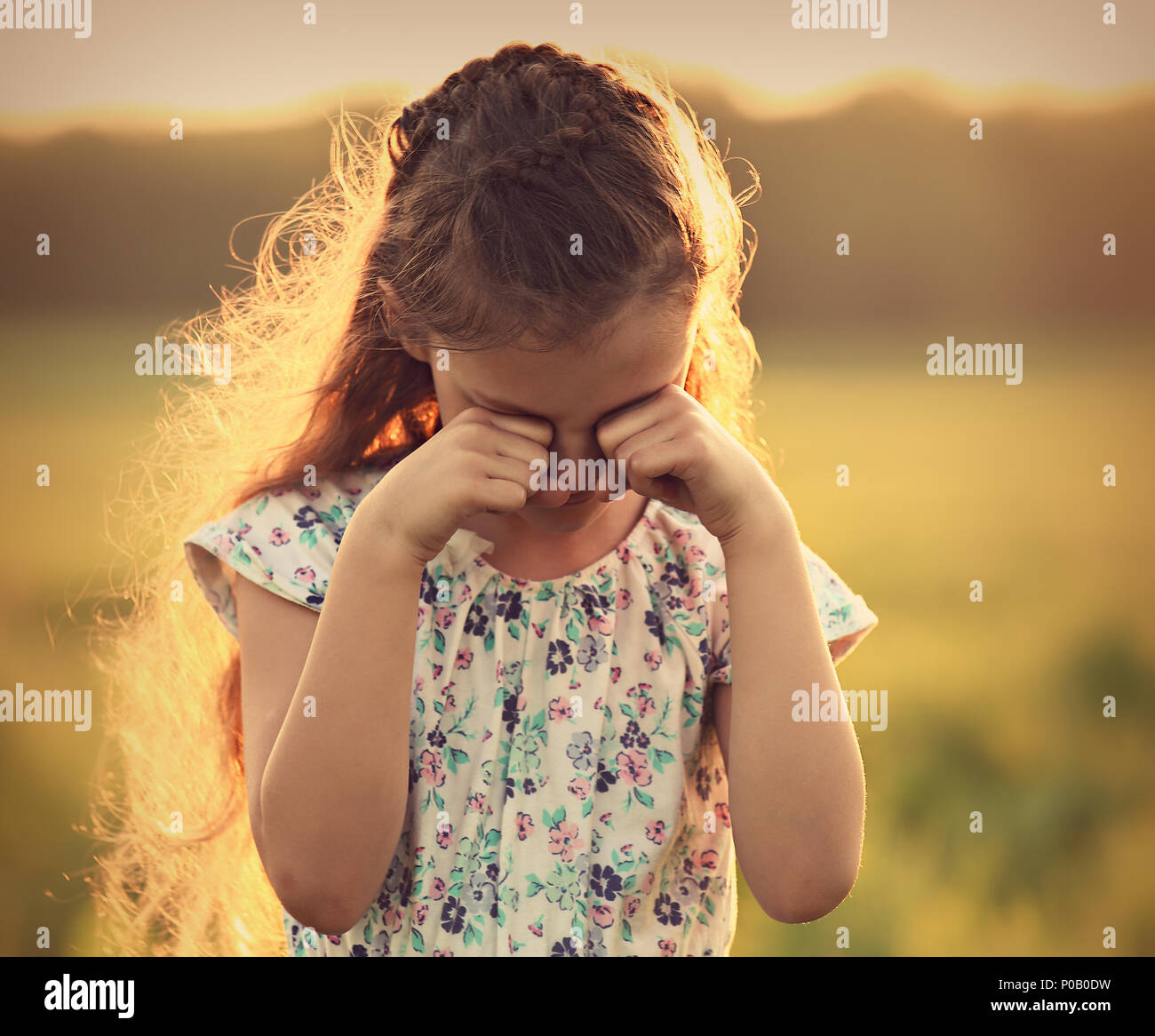 Crying unhappy alone kid girl covering face the hands on summer nature ...