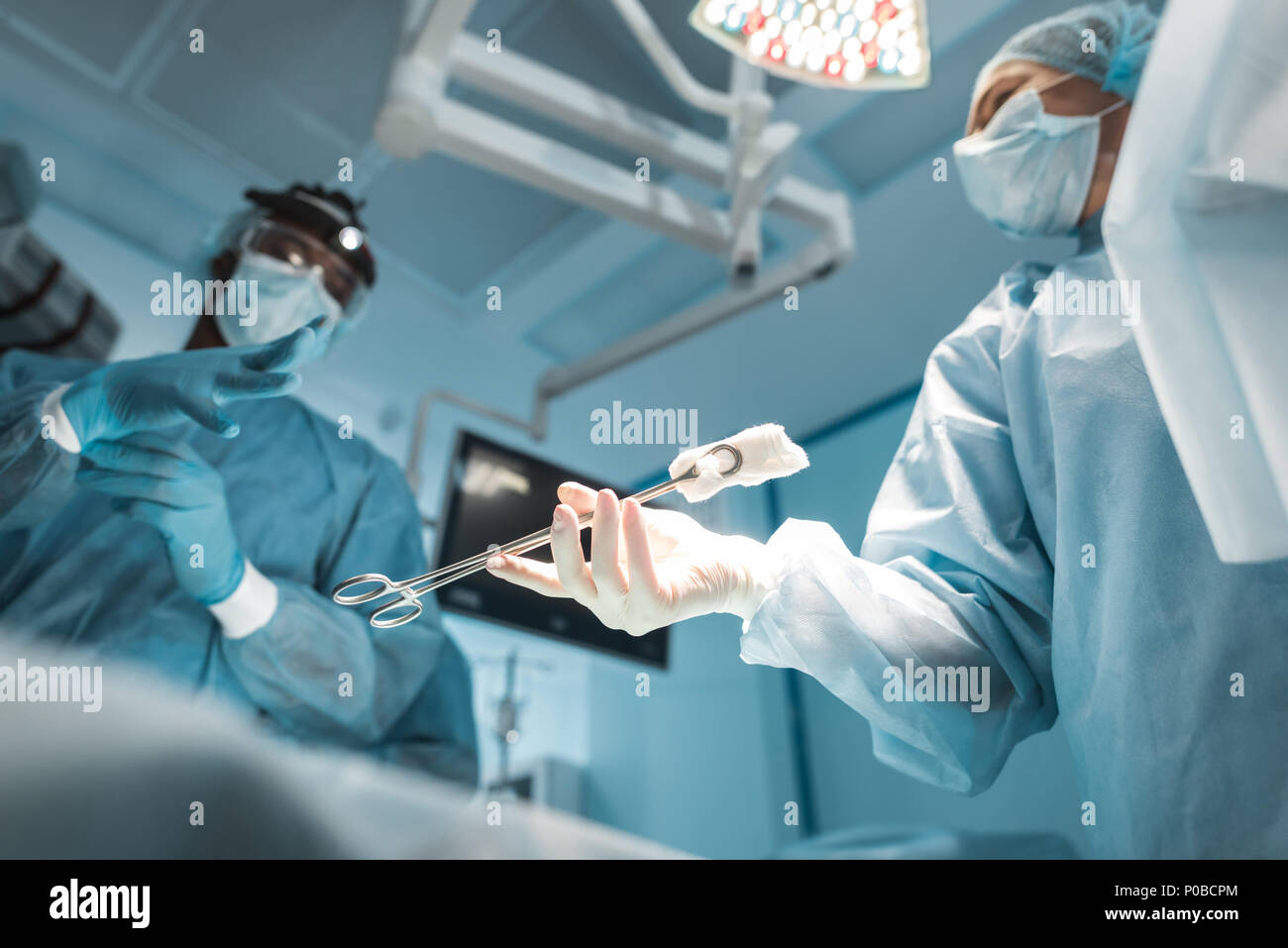 bottom view of doctor passing medical clamp to african american surgeon ...
