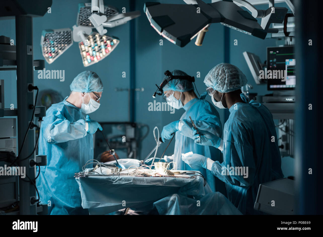 side view of multicultural surgeons operating patient in operating room ...