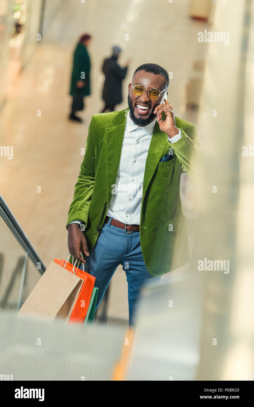 happy stylish man on escalator at shopping mall and talking by phone ...