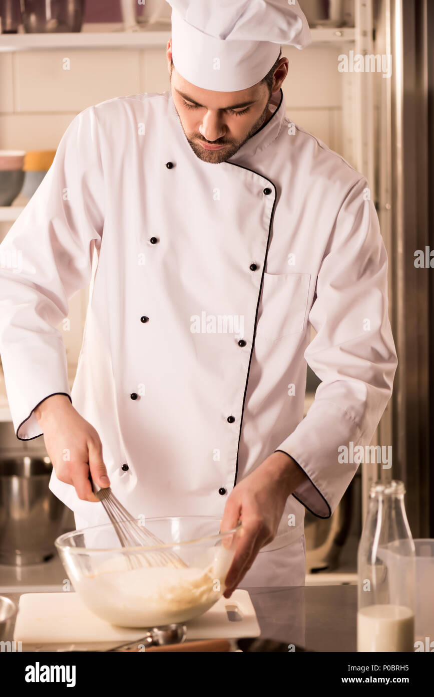 focused confectioner in chef hat making dough in restaurant kitchen ...