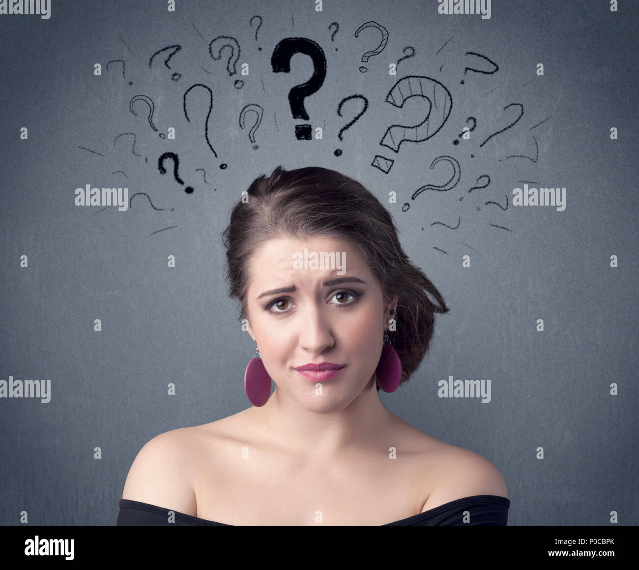 A pretty teenage girl standing confused in front of grey wall ...