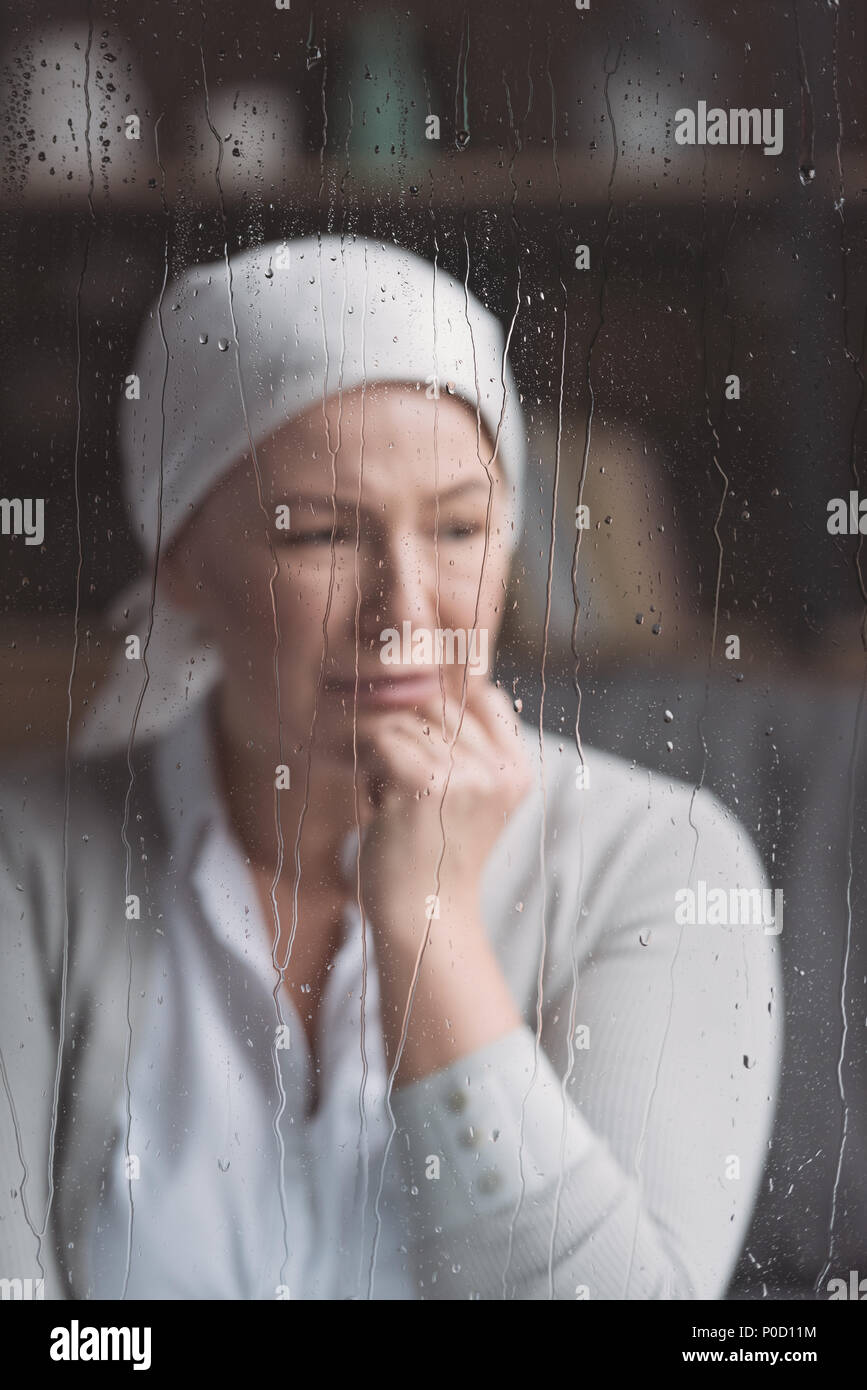 sick mature woman in kerchief crying behind window with raindrops Stock ...