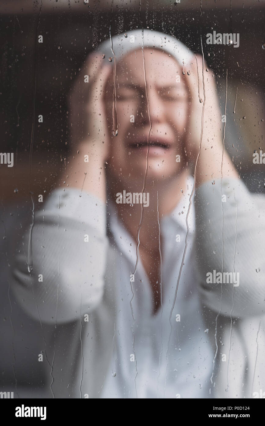 sick mature woman in kerchief crying behind window with raindrops Stock ...