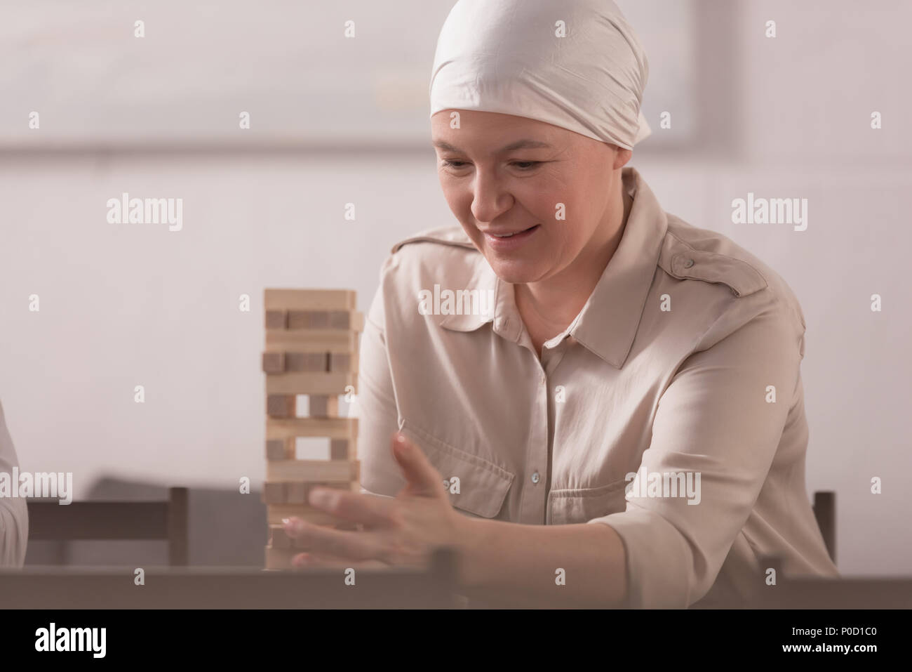 sick smiling mature woman in kerchief building tower from wooden blocks ...