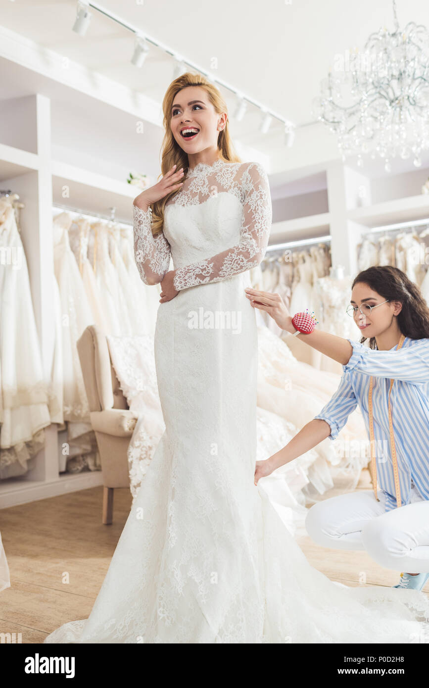 Blonde bride in lace dress and tailor during dress fitting in wedding ...