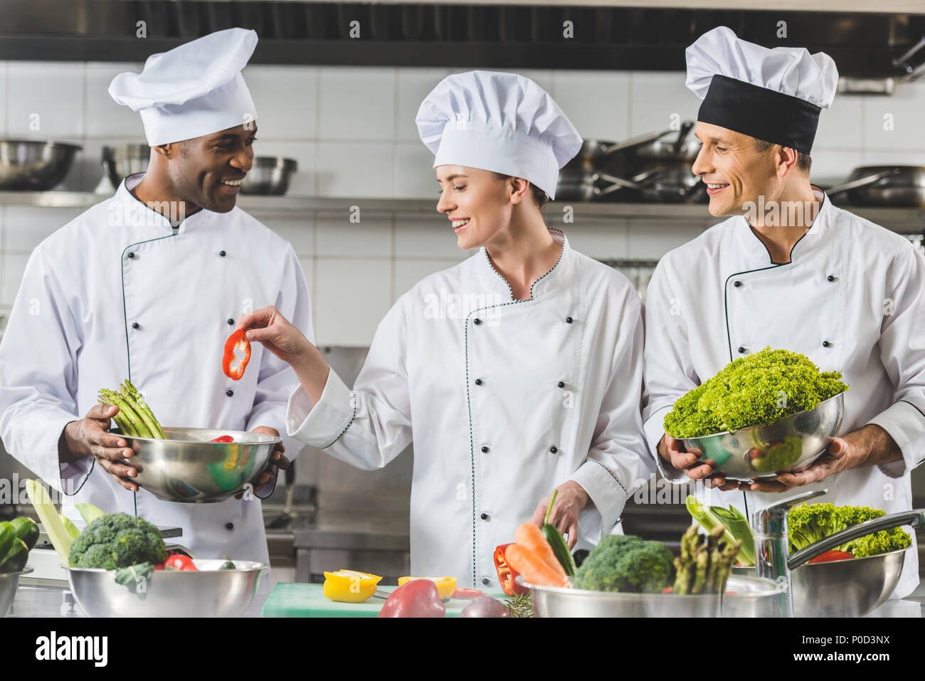 happy multicultural chefs cooking vegetables at restaurant kitchen ...