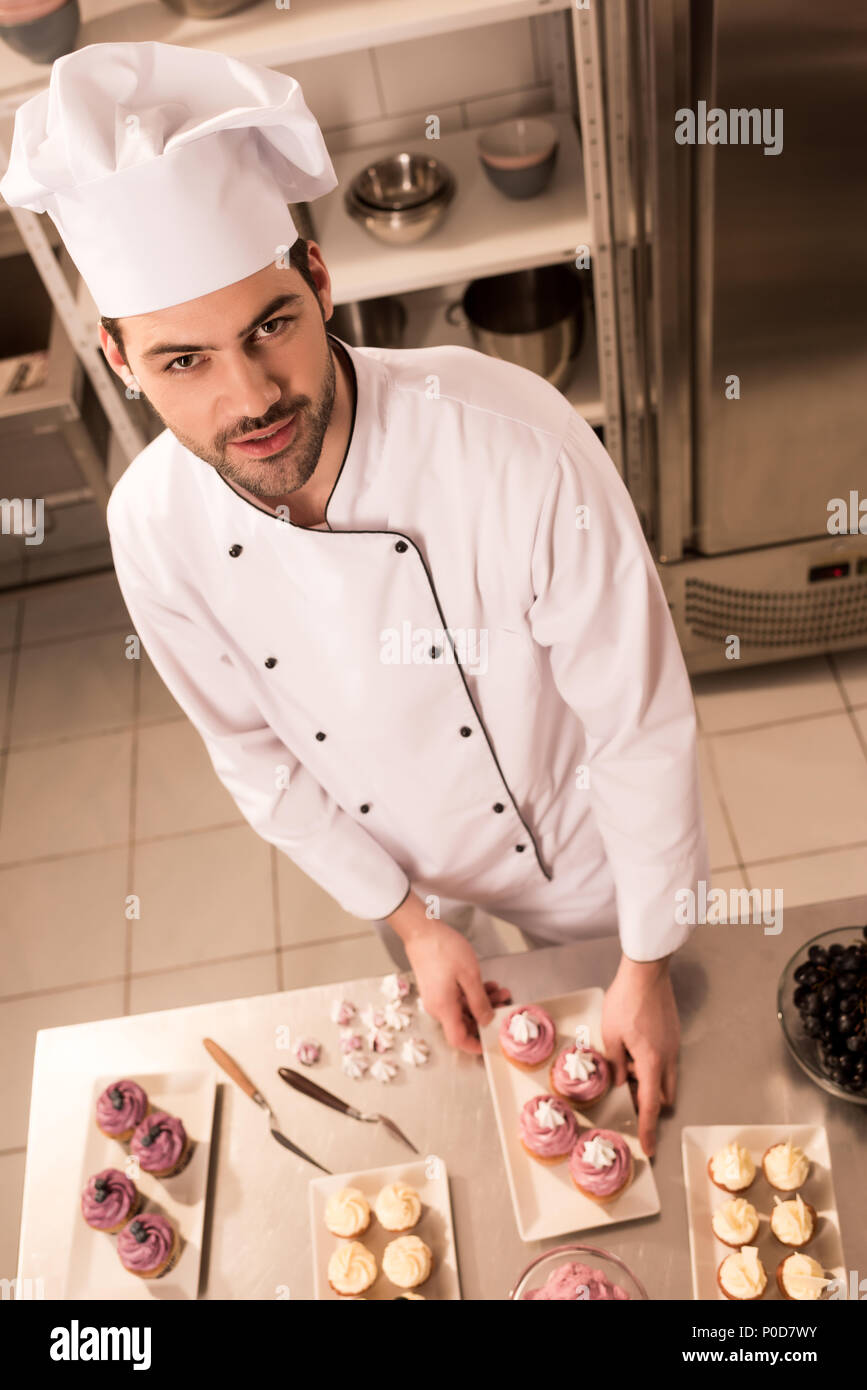 high angle view of confectioner in chef hat standing at counter with ...