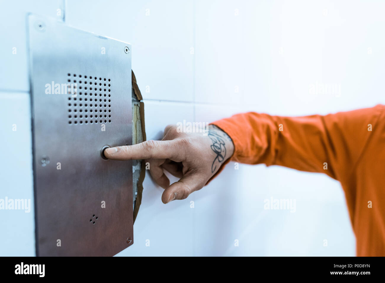 cropped image of tattooed prisoner in orange uniform pressing button in ...