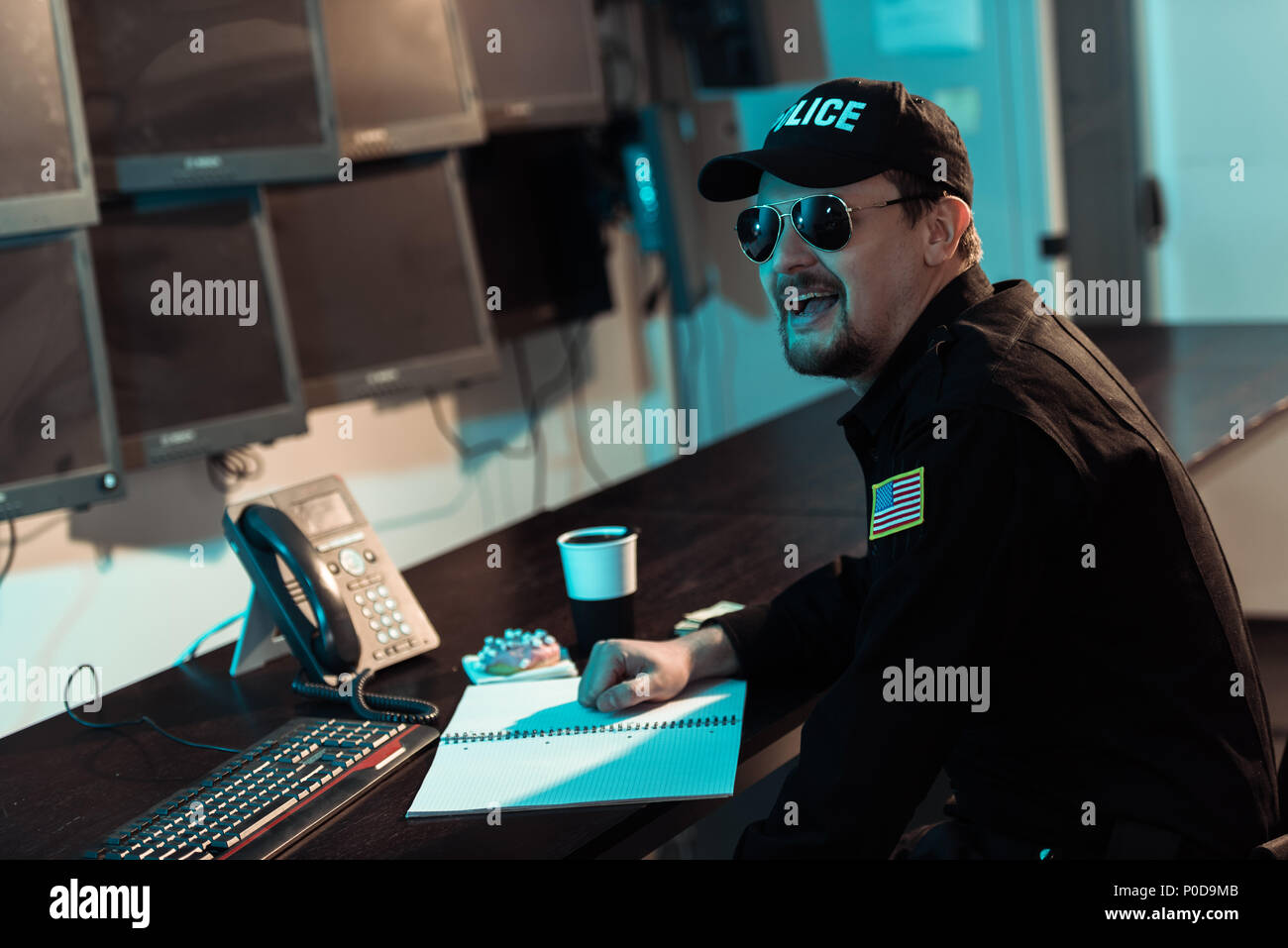 laughing prison guard sitting at working table and monitoring people in ...
