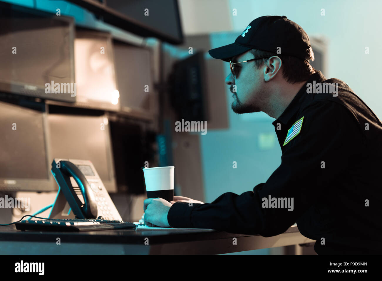 side view of prison guard sitting with cup of coffee and monitoring ...