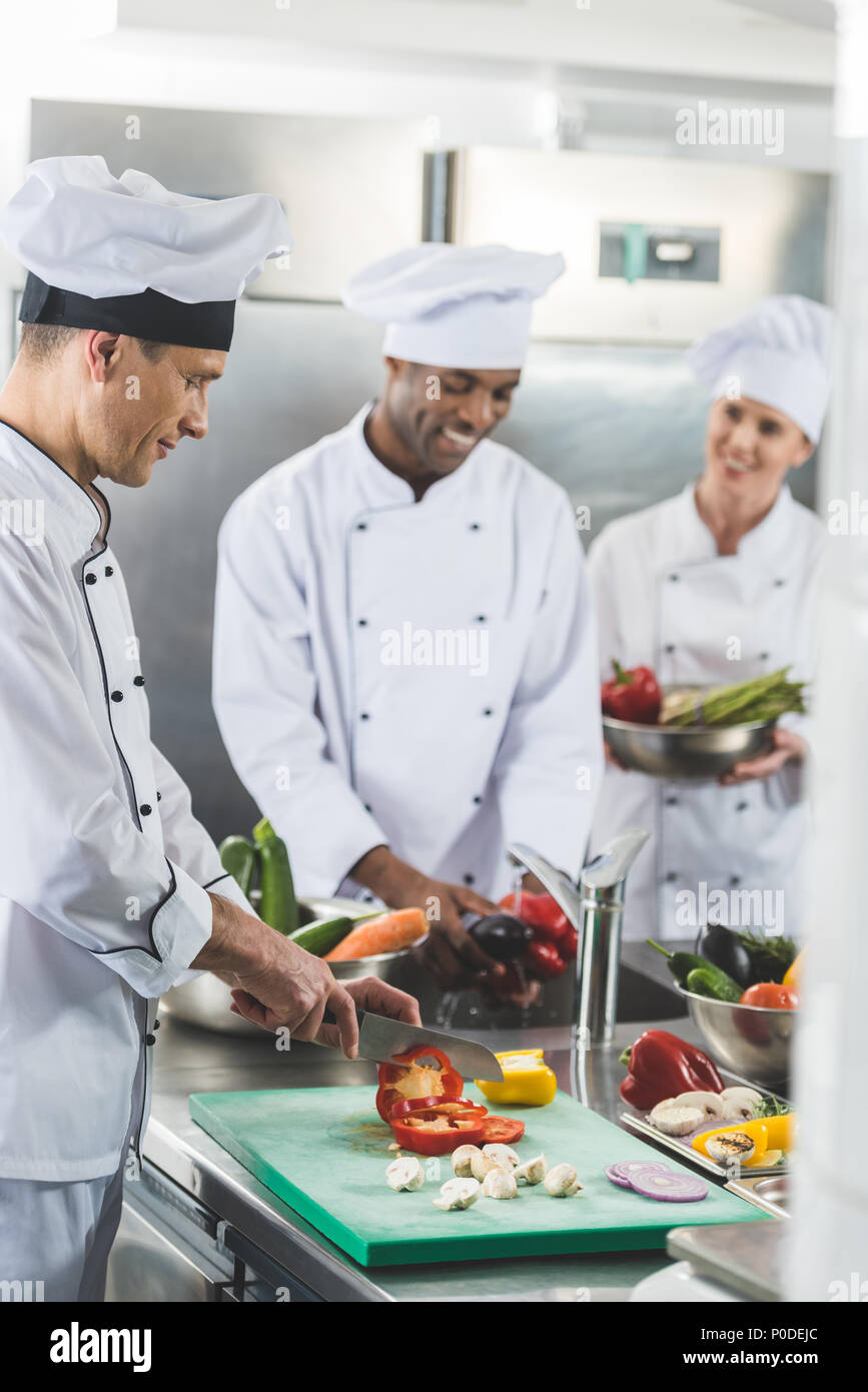 happy multicultural chefs preparing vegetables at restaurant kitchen ...