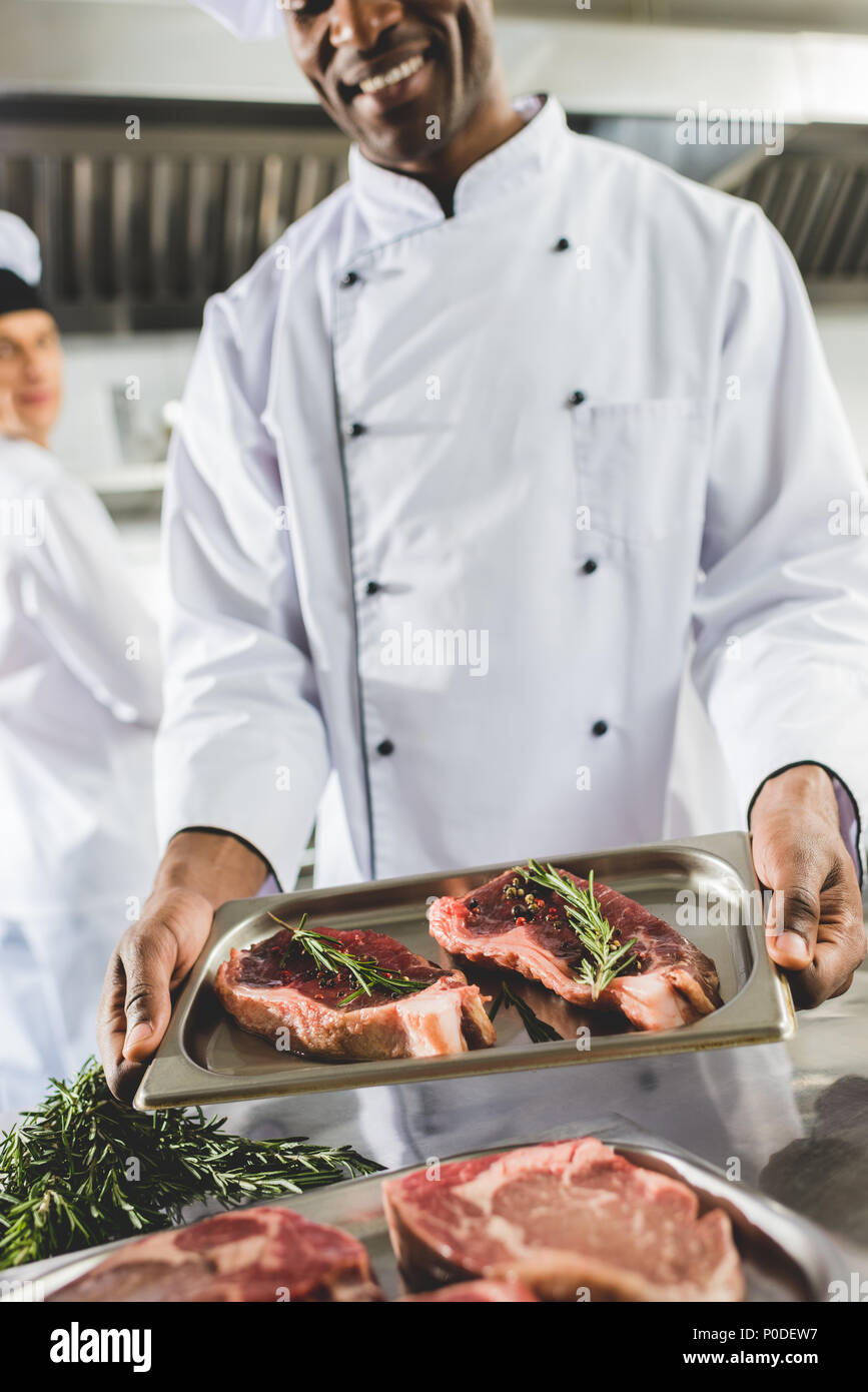 african american chef holding tray with raw meat at restaurant kitchen ...