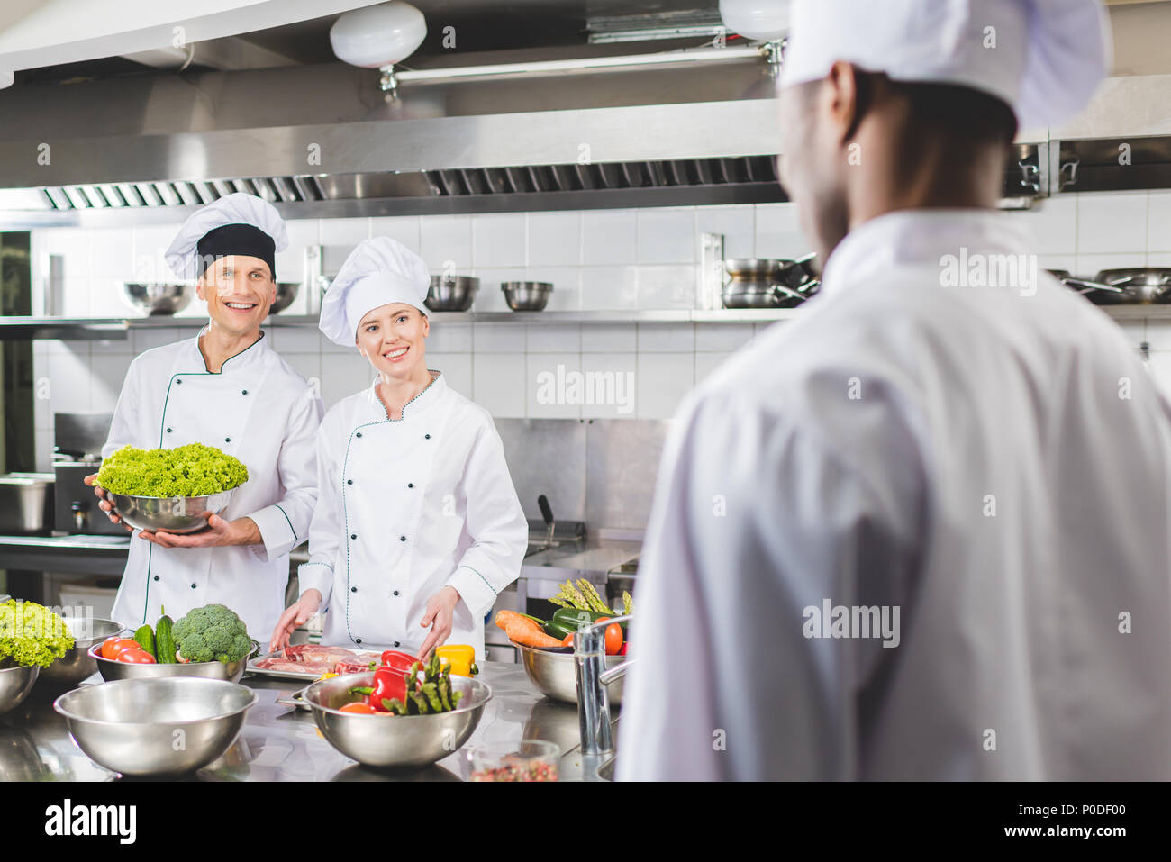 smiling multicultural chefs looking at each other at restaurant kitchen ...