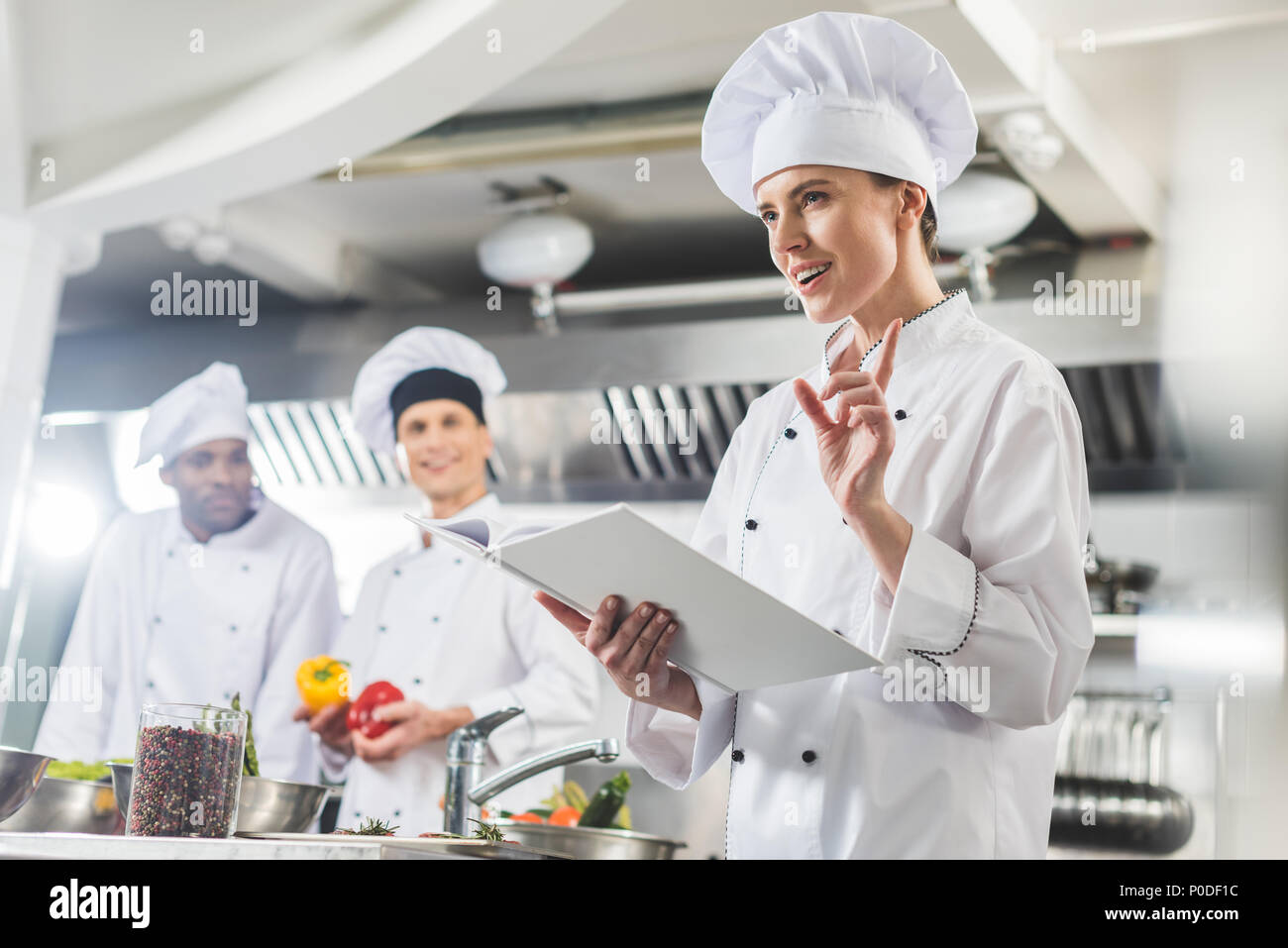 attractive chef holding recipe book and showing idea gesture at ...