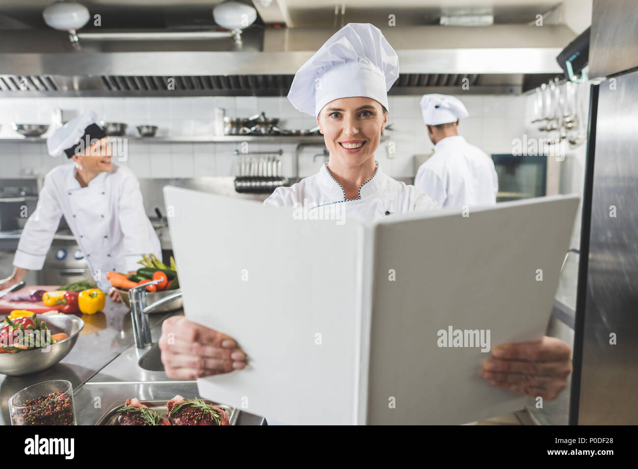 happy chef holding recipe book at restaurant kitchen Stock Photo - Alamy